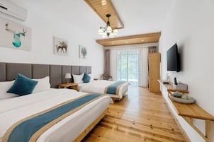 Quarto de hotel com duas camas, chão de madeira, televisão e obras de arte nas paredes.