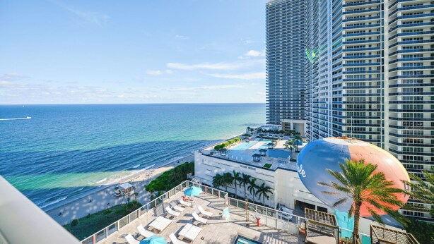 Hotel alto com piscina no terraço e vista para o oceano.