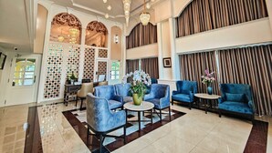 Um hall amplo com poltronas azuis, um candelabro e uma grande janela com cortinas.
