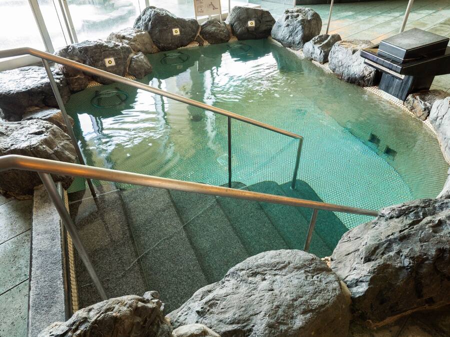 Uma área de águas termais com piscina, grades de metal e pedras grandes.