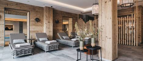 Uma área de spa moderna com paredes de madeira, cadeiras de descanso e uma pequena mesa com plantas em vasos.