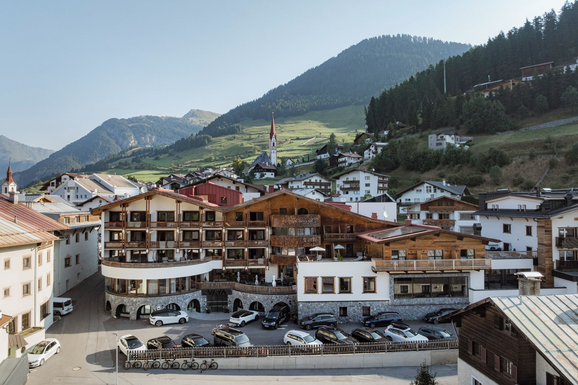 Um hotel com vários andares, área de estacionamento e vista para a paisagem montanhosa ao redor.