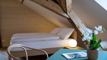 Um quarto pequeno e acolhedor com uma cama de solteiro, uma mesa de cabeceira com abajur e uma cadeira.
