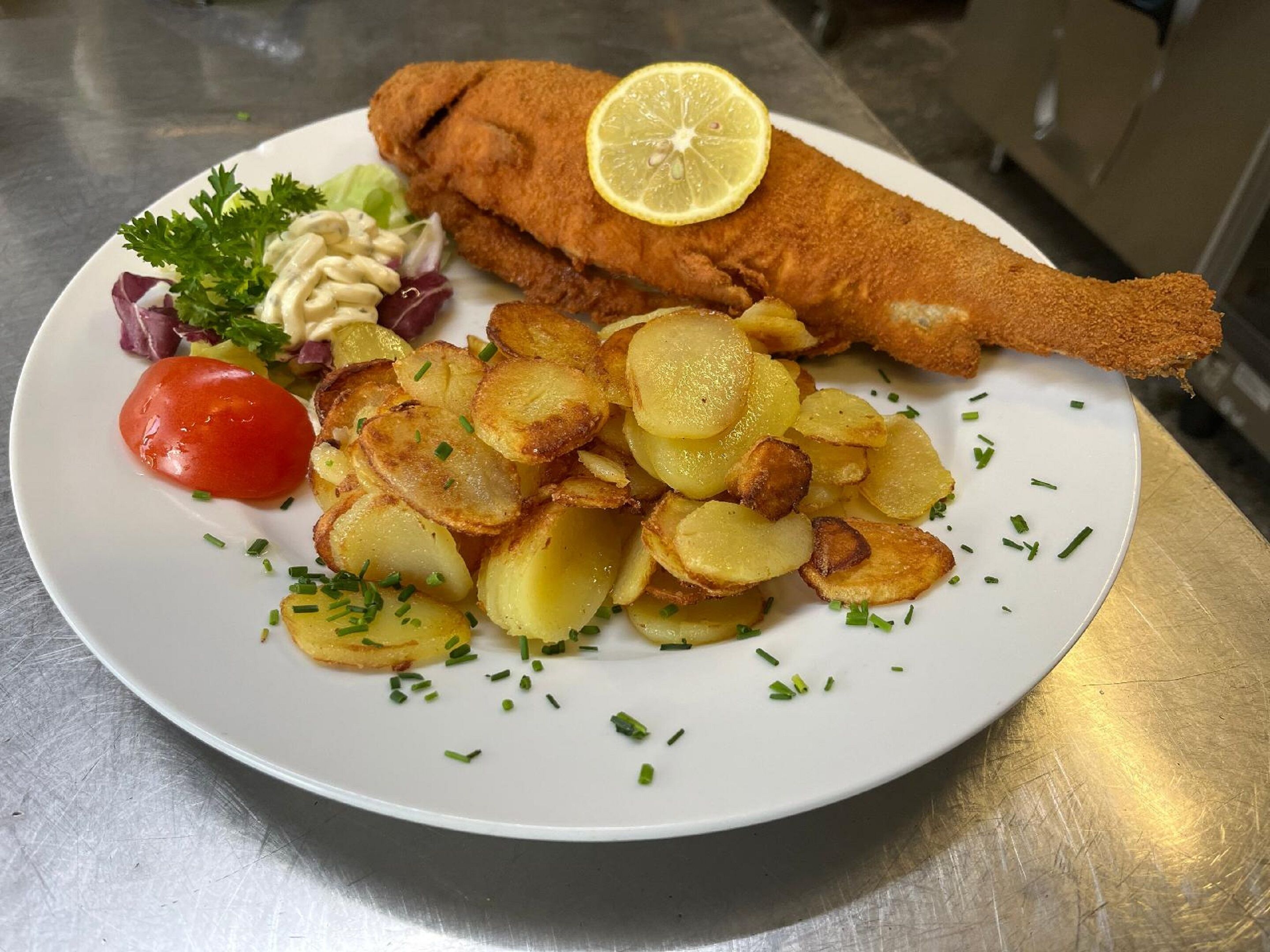 Um prato com um filé de peixe empanado, batatas rústicas, um tomate cereja e uma salada.