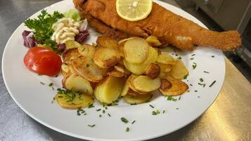 Um prato com um filé de peixe empanado, batatas rústicas, um tomate cereja e uma salada.