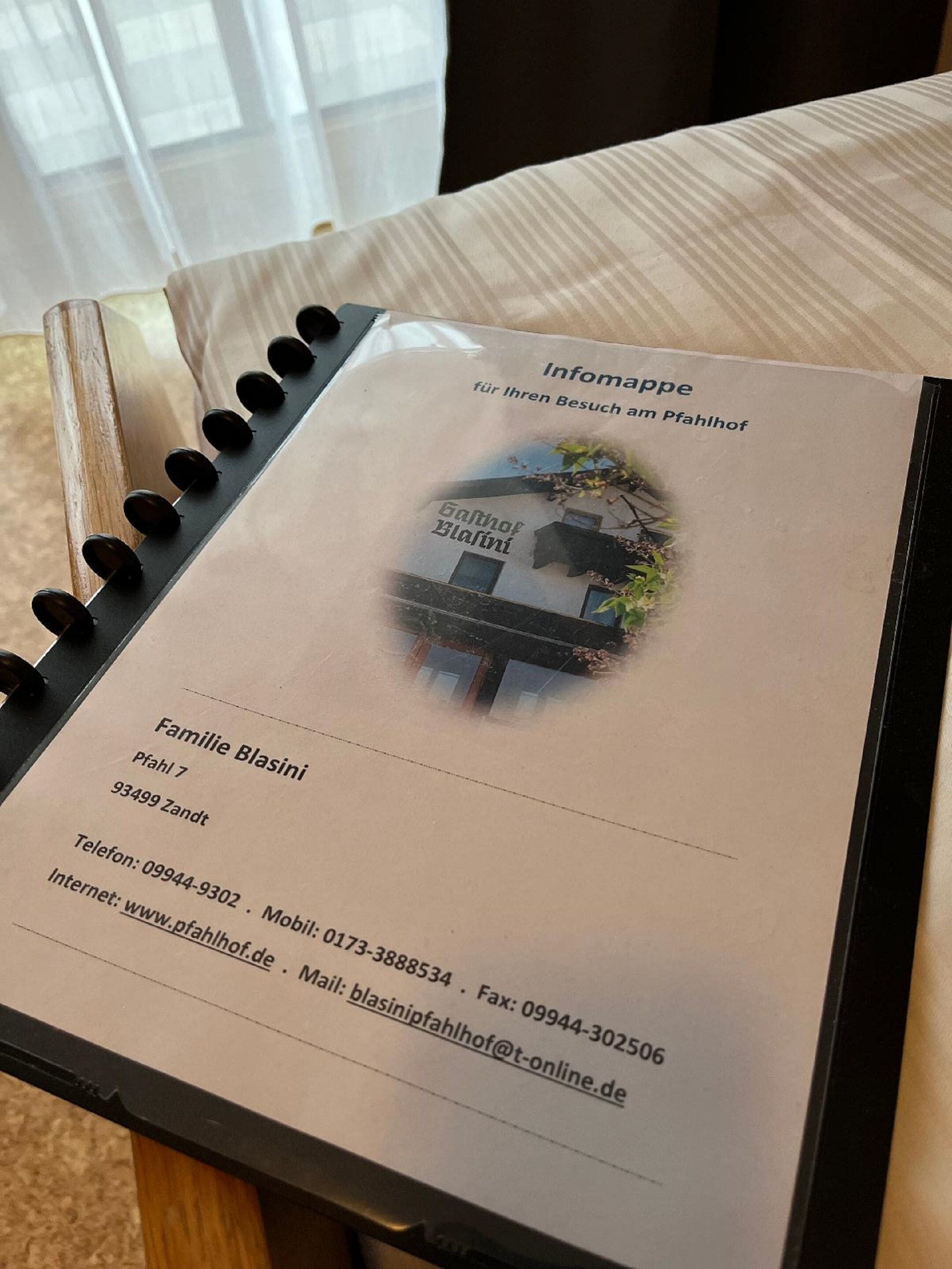 Um folheto do hotel 'Familie Blasini' com informações de contacto, incluindo número de telefone, número de telemóvel e endereço de email.