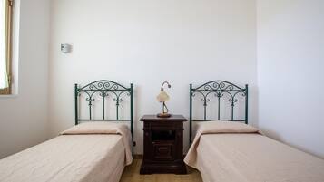 Quarto com duas camas de solteiro, mesa de cabeceira com abajur e tomada na parede.