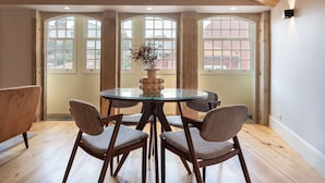 Uma sala de jantar com uma mesa de vidro redonda, quatro cadeiras e um vaso com flores secas.