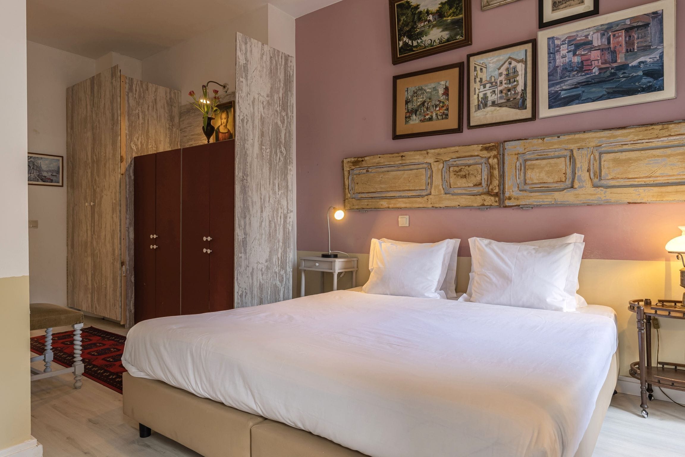 Quarto com uma cama grande, guarda-roupa, mesa de cabeceira e parede com quadros.