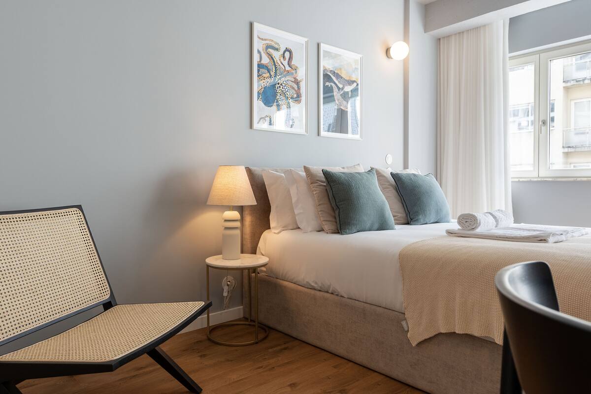 Quarto de hotel com cama, uma poltrona, abajur e duas obras de arte na parede.