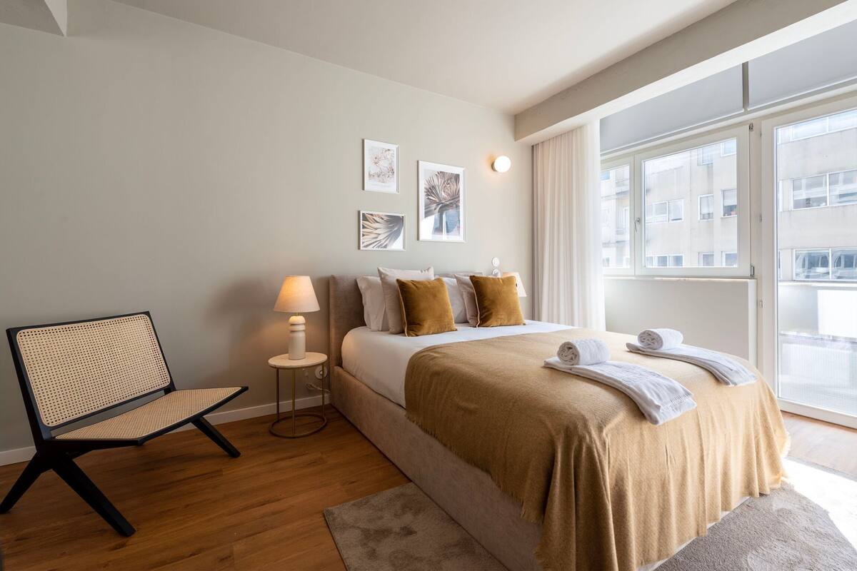 Um quarto moderno com uma cama grande, uma mesinha de cabeceira, uma cadeira e obras de arte na parede.