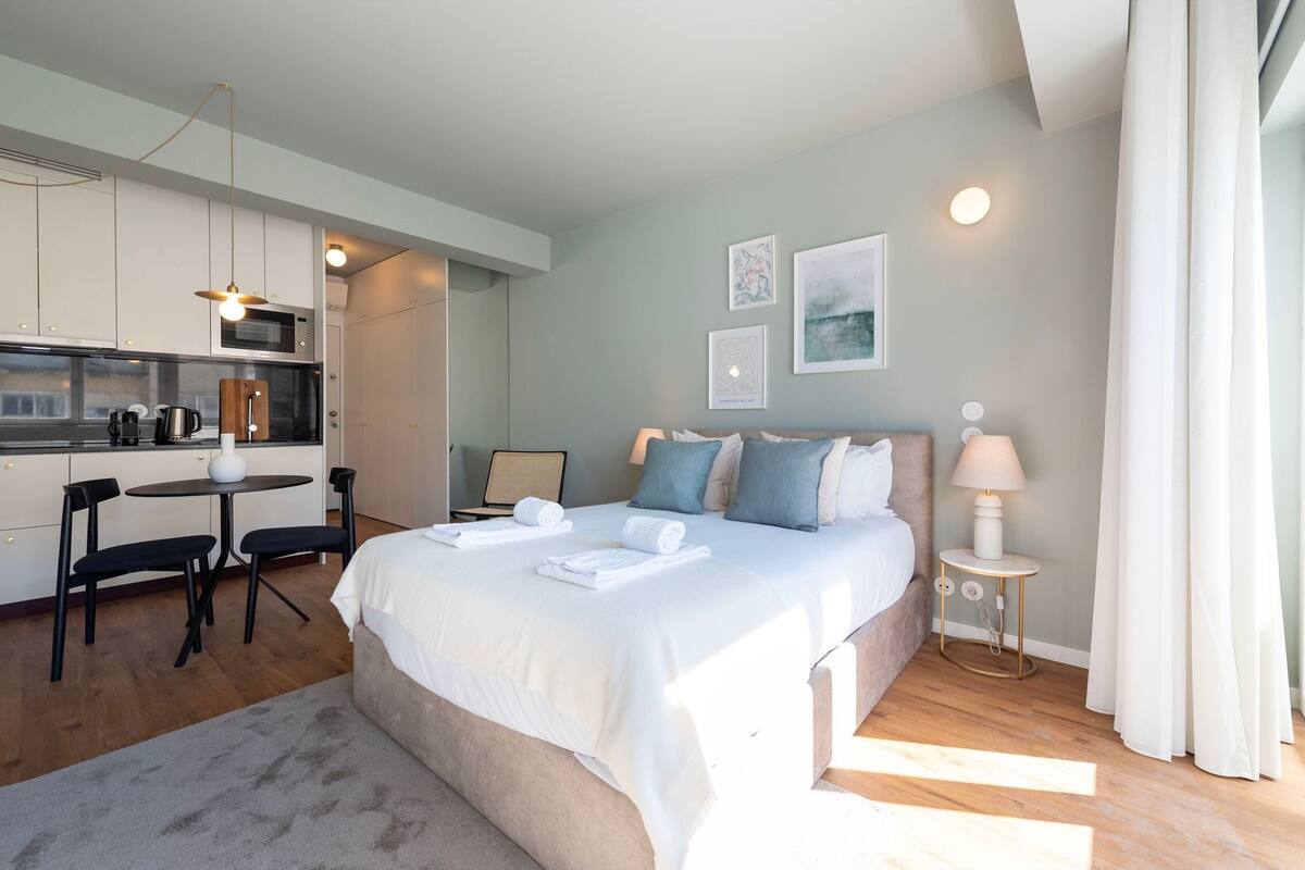 Quarto de hotel moderno com uma cama grande, uma pequena área de cozinha e uma mesa de jantar.