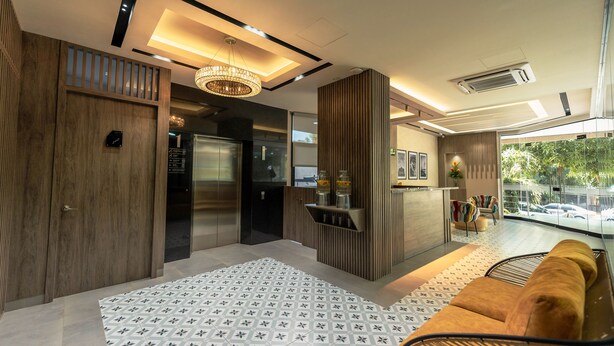 Um hall de hotel moderno com piso estampado, uma área de estar central e um balcão de recepção.