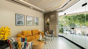 Uma sala de estar moderna com um sofá, uma poltrona colorida, uma mesa de centro de vidro e quadros nas paredes.