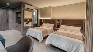 Quarto de hotel moderno com duas camas, um espaço de estar e um espelho.