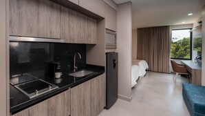 Cozinha moderna com fogão embutido, pia e geladeira, quarto com cama e janela, e área de estar com mesa e cadeiras.