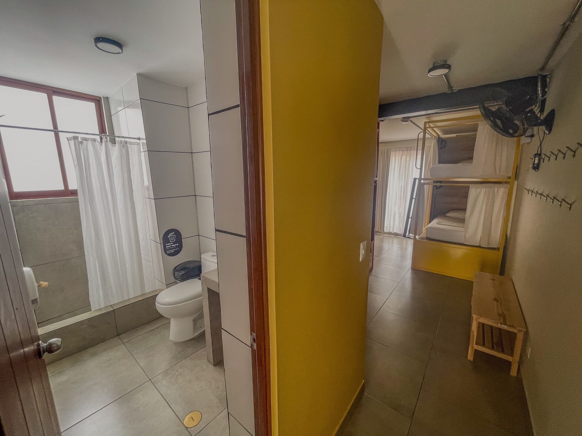 Quarto pequeno com vaso sanitário, um banquinho de madeira e uma cama beliche com colchão.
