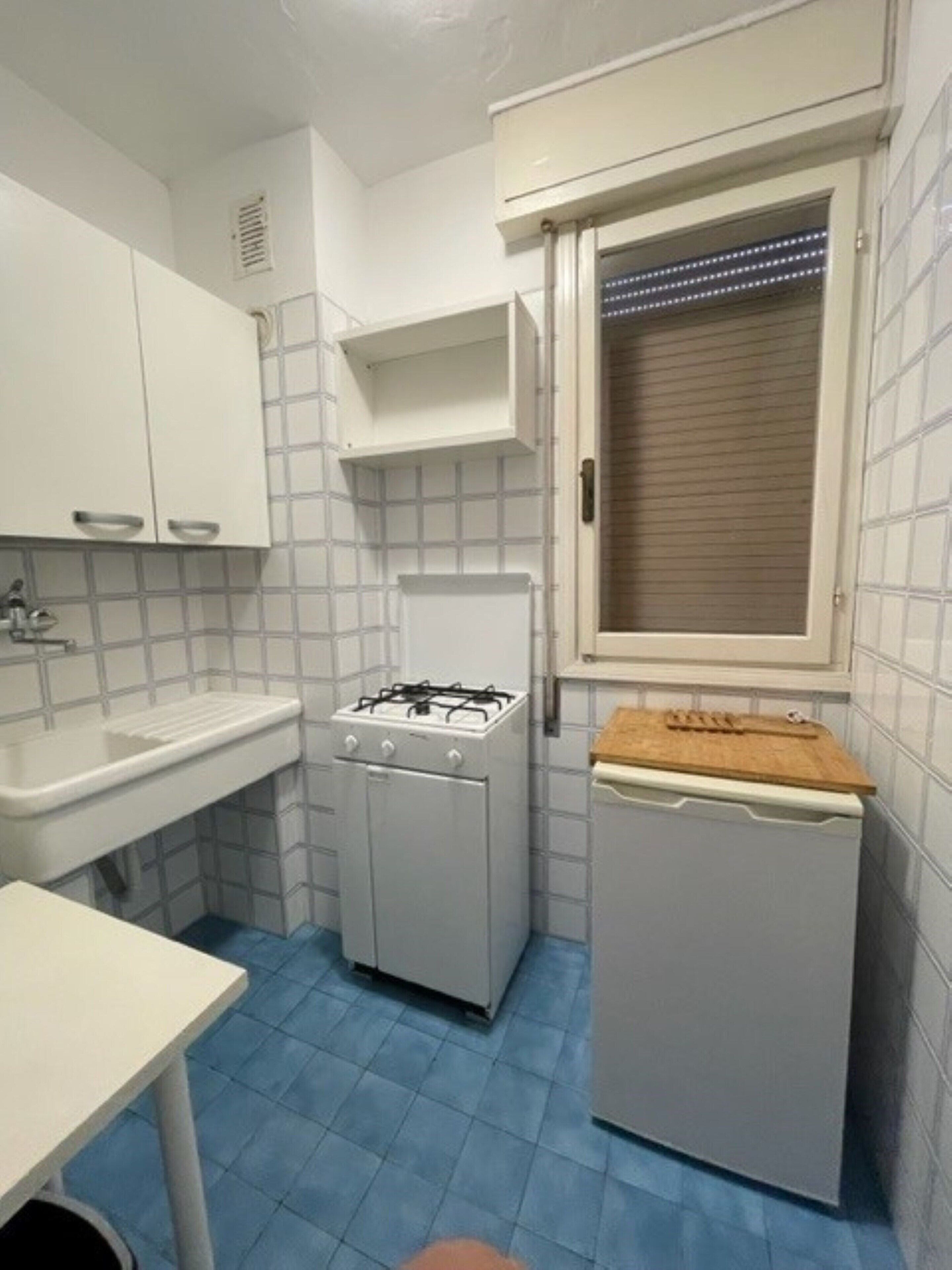 Uma cozinha compacta com fogão a gás, um refrigerador pequeno, uma pia e uma janela com persianas.