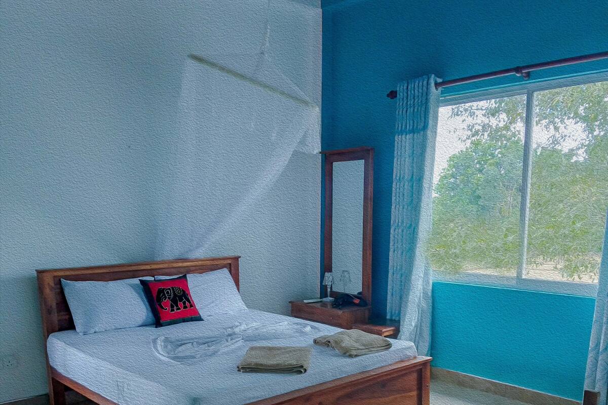 Quarto com cama de madeira, mesa de cabeceira, espelho e janela com vista para vegetação.