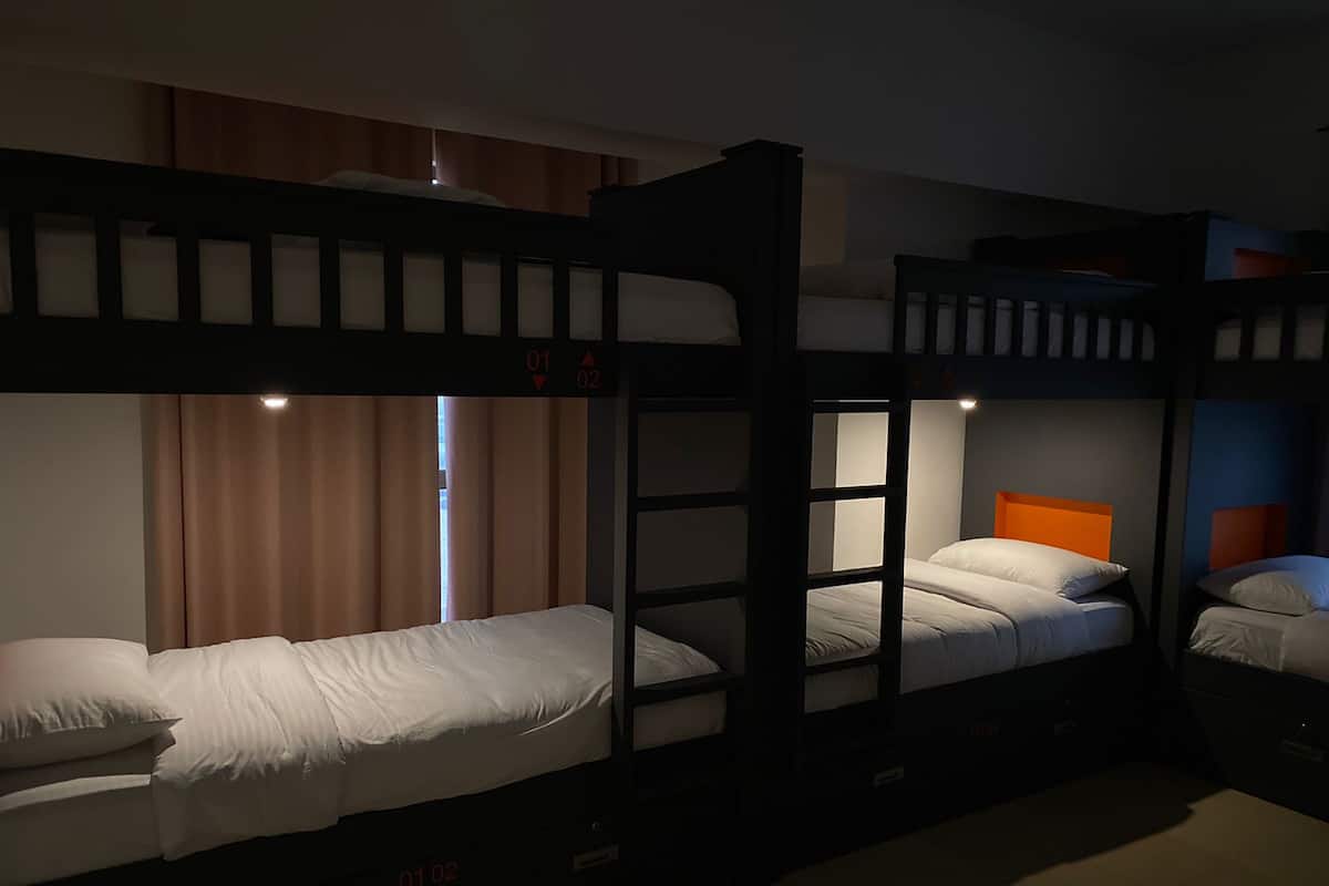 Quarto com beliche, janela, cortinas e mesa de cabeceira.