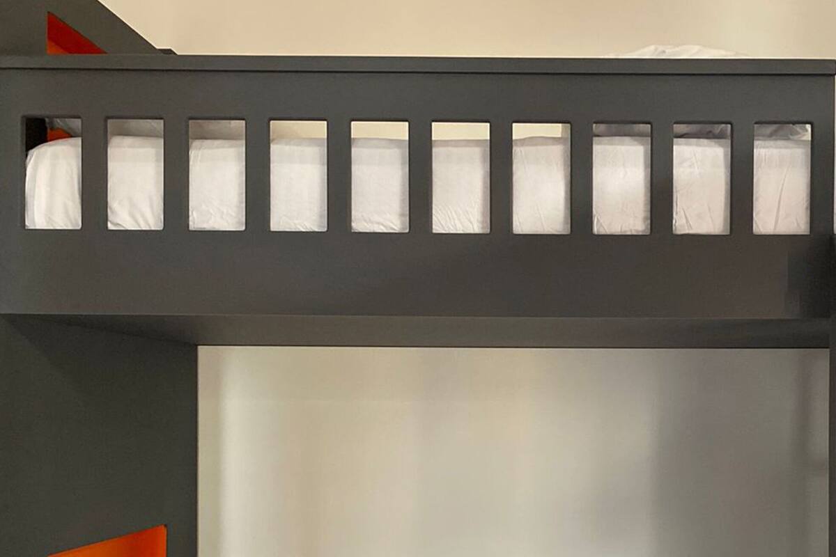 Uma cama beliche com prateleira na parte de baixo e uma cama de solteiro em cima.