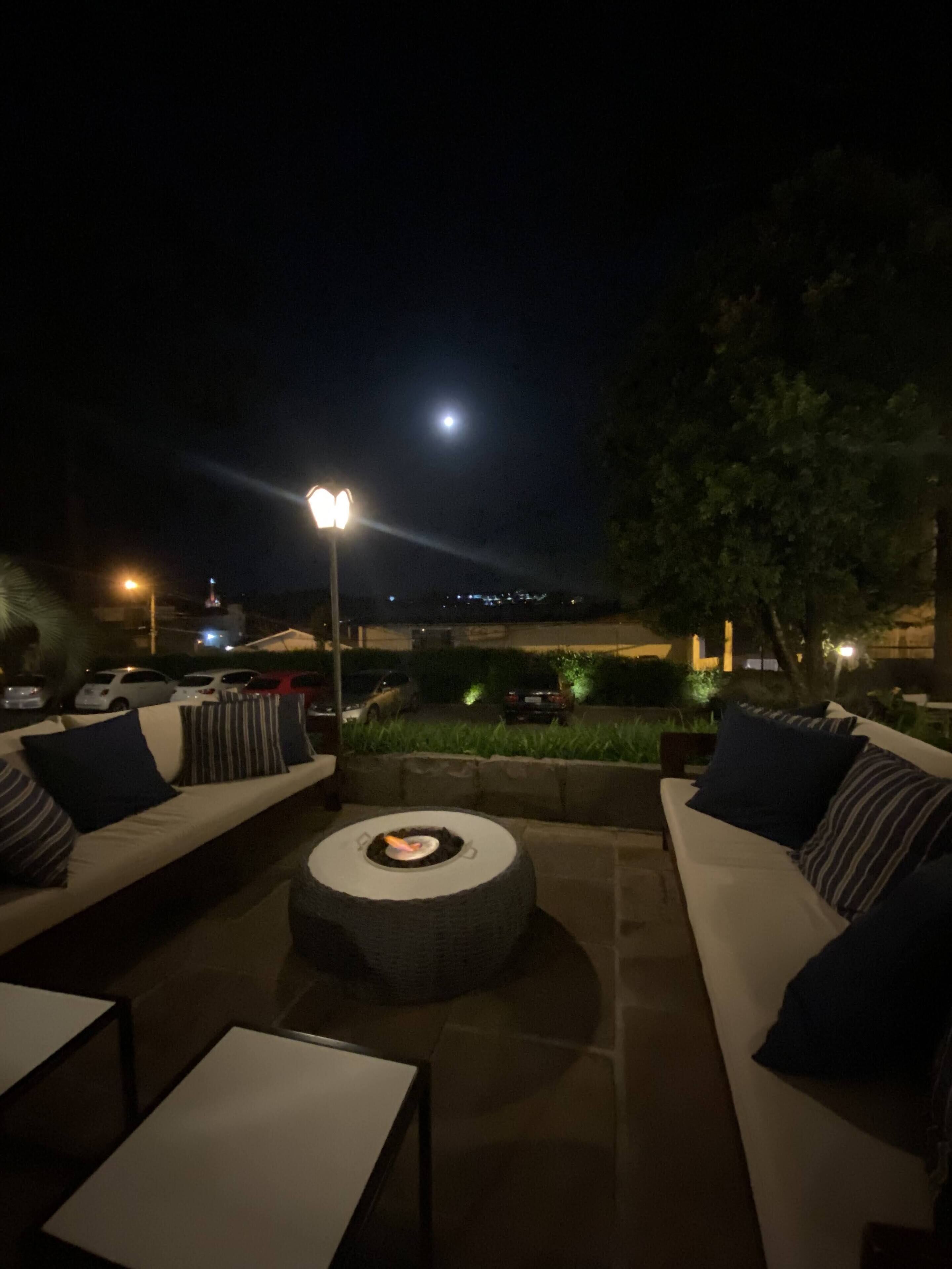 Uma área externa com assento, incluindo uma mesa redonda e dois sofás, um poste de luz e vista para a lua.