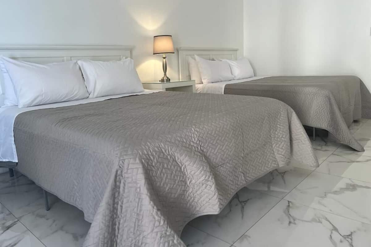 Quarto de hotel com duas camas, mesa de cabeceira com abajur e piso de mármore.