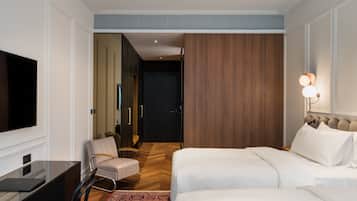 Quarto de hotel com cama, escrivaninha, cadeira, televisão e porta que dá para um corredor.