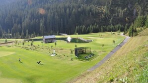 Um campo de golfe com lago, plataforma de observação e um edifício ao fundo.