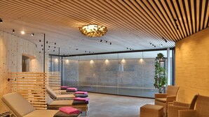 Espaço de spa com paredes de ripas de madeira, espreguiçadeiras e uma janela ampla com vista para um muro de tijolos.