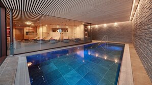 Piscina interior moderna com teto de madeira e paredes de tijolo.