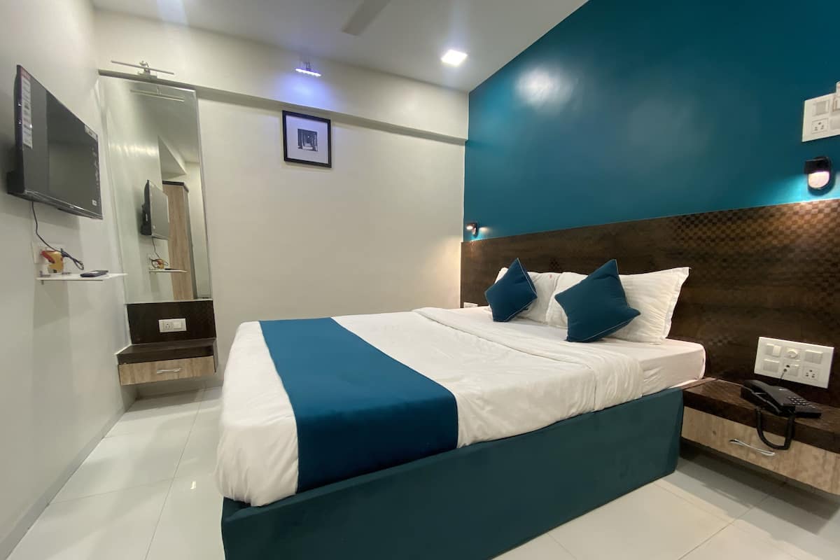 Quarto de hotel moderno com uma cama grande, mesa de cabeceira com telefone, espelho e televisão de tela plana na parede.