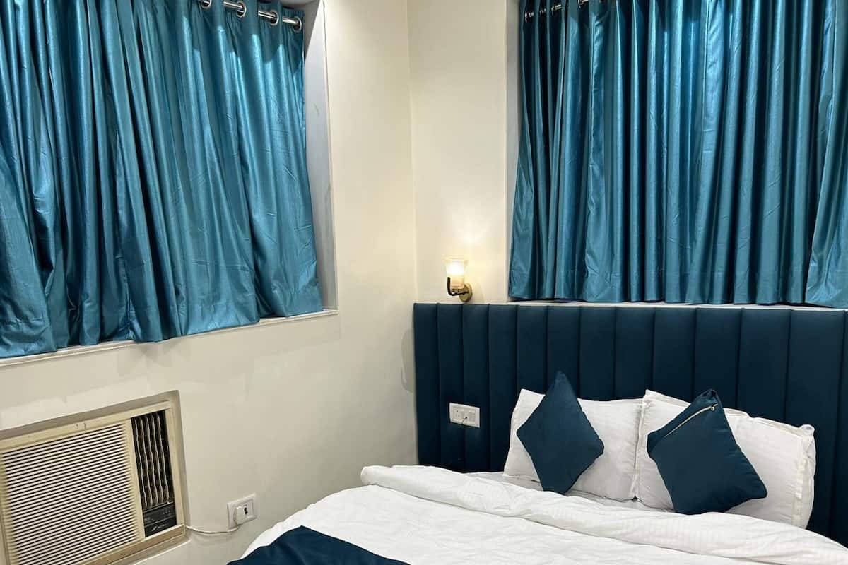 Quarto de hotel com cama, cortinas azuis, luminária na parede e um respiradouro.