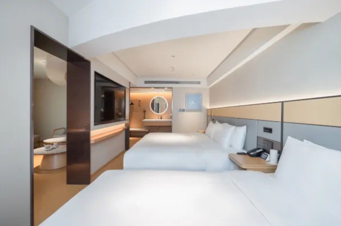 Quarto de hotel com duas camas, banheiro, televisão e mesa de cabeceira com telefone.