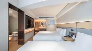 Quarto de hotel com duas camas, banheiro, televisão e mesa de cabeceira com telefone.