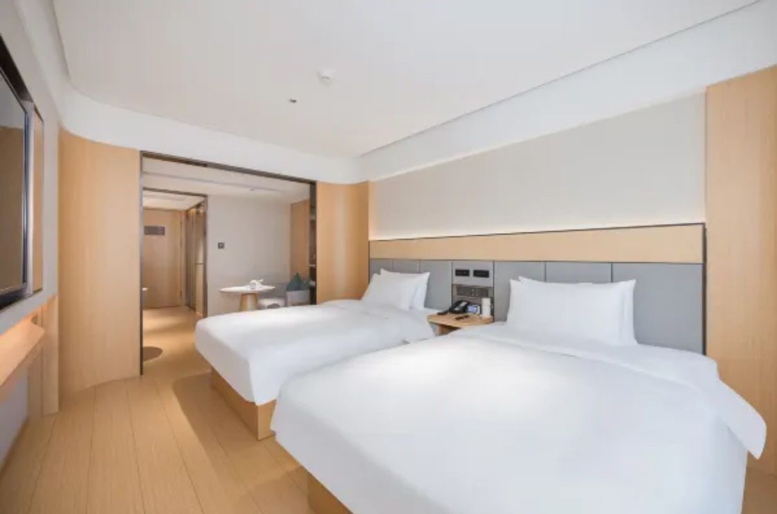 Quarto de hotel com duas camas, uma mesa de cabeceira com telefone e uma pequena mesa com uma cadeira.