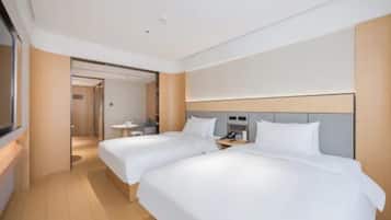 Quarto de hotel com duas camas, uma mesa de cabeceira com telefone e uma pequena mesa com uma cadeira.