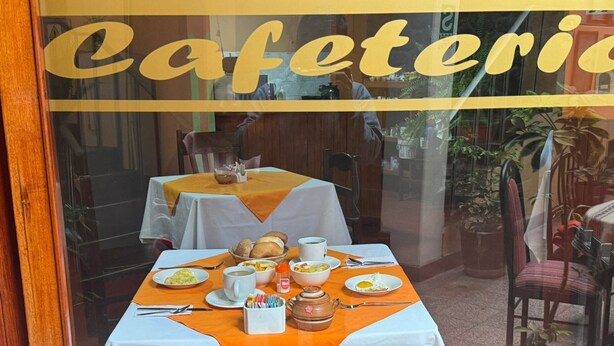 Janela de restaurante com mesas montadas para o café da manhã, incluindo pratos de comida, xícaras e uma cafeteira.