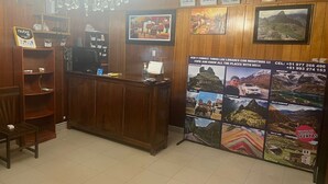 Uma área de recepção com uma mesa de madeira, um candelabro, quadros nas paredes e um mural com cartazes de viagens.