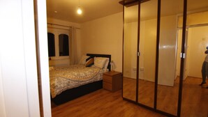Quarto com cama, mesa de cabeceira, abajur, guarda-roupa e janela.