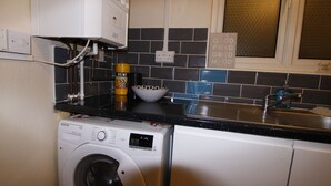 Cozinha compacta com máquina de lavar, uma tigela e uma garrafa de detergente no balcão.