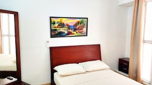 Quarto de hotel com cama, mesa de cabeceira, um quadro na parede e janela com cortinas.