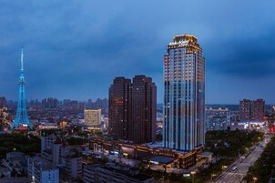 Um hotel alto com um letreiro chamativo da "Four Points", cercado por outros edifícios e uma torre iluminada em azul ao fundo.