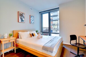 Quarto de hotel moderno com uma cama grande, uma escrivaninha e uma janela com vista para a cidade.