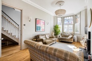Sala de estar ampla com escada, uma grande janela com persianas e um lustre moderno.
