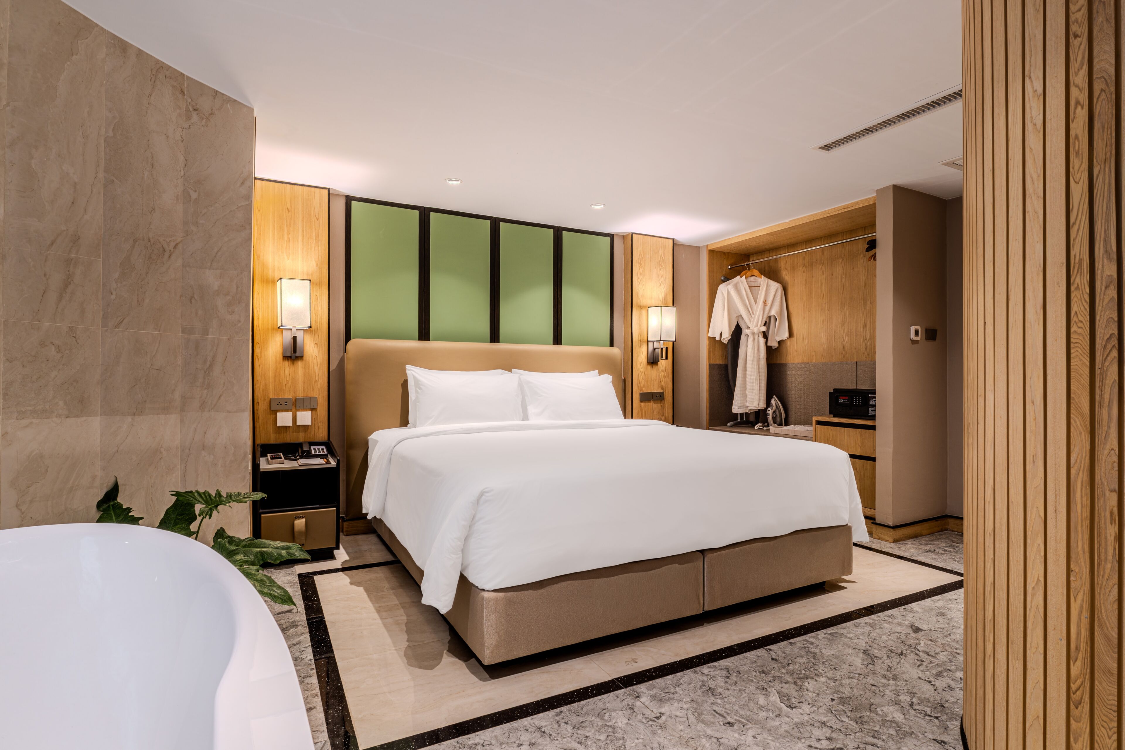 Quarto de hotel moderno com uma cama grande, um banheiro com banheira e um guarda-roupa de madeira.