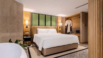 Quarto de hotel moderno com uma cama grande, um banheiro com banheira e um guarda-roupa de madeira.