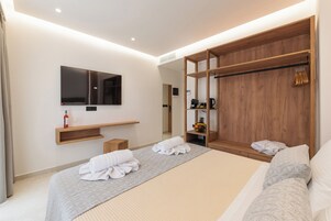Quarto de hotel moderno com uma cama grande, uma televisão de tela plana, um guarda-roupa de madeira e uma pequena prateleira com artigos de higiene pessoal.