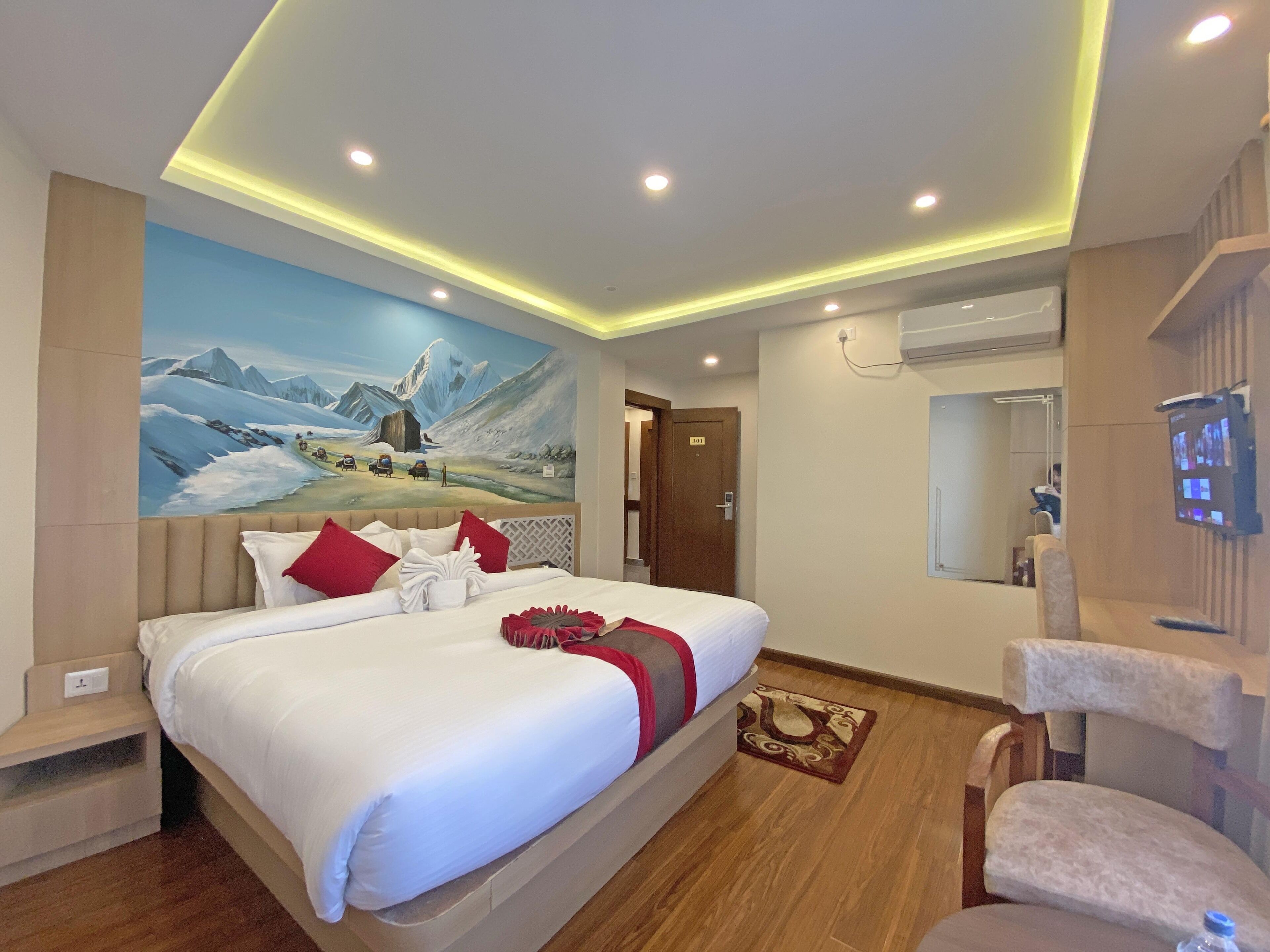 Quarto de hotel moderno com uma cama grande, uma televisão montada e um mural de uma paisagem montanhosa.