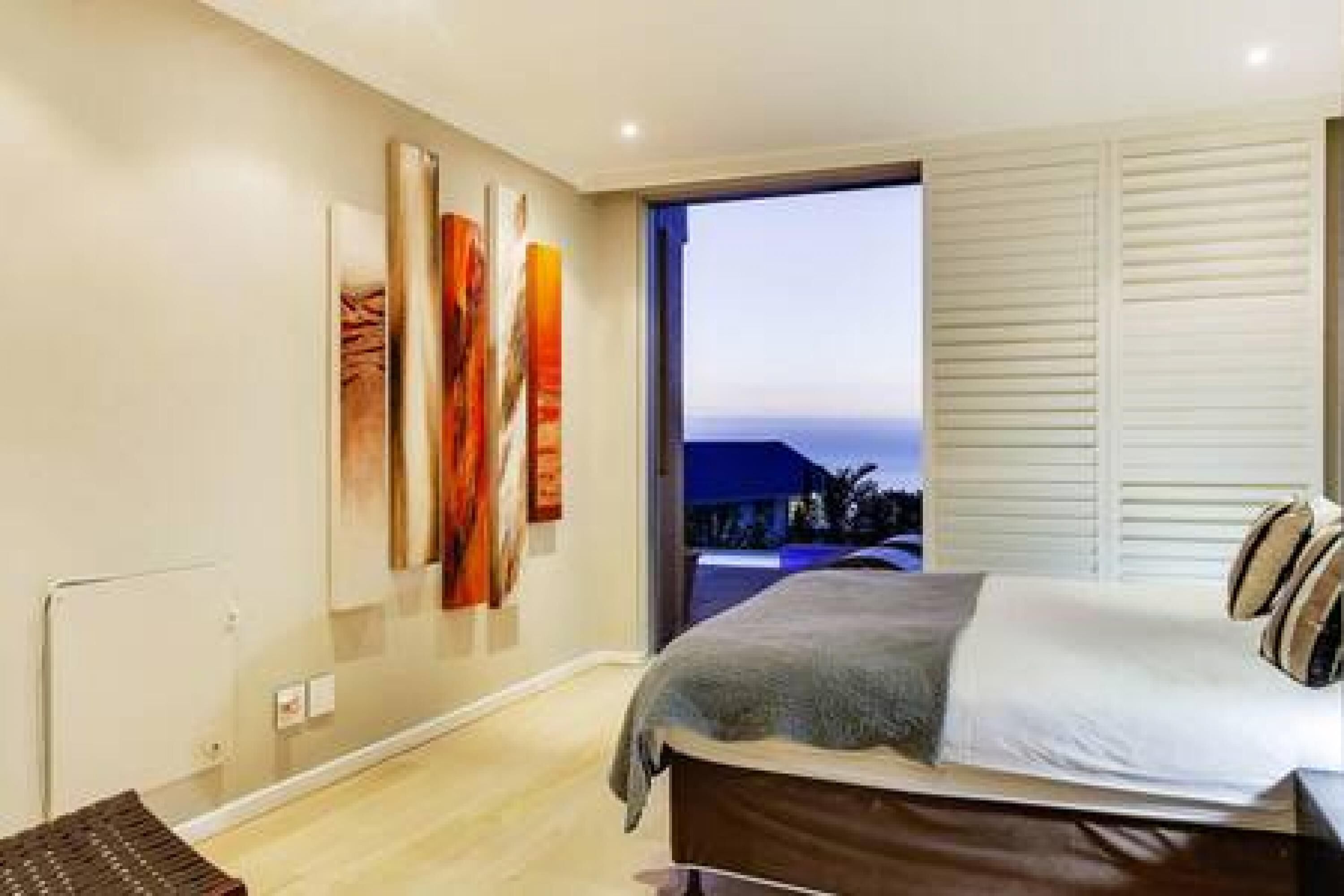 Quarto moderno com cama grande, vista para o oceano e arte abstrata nas paredes.